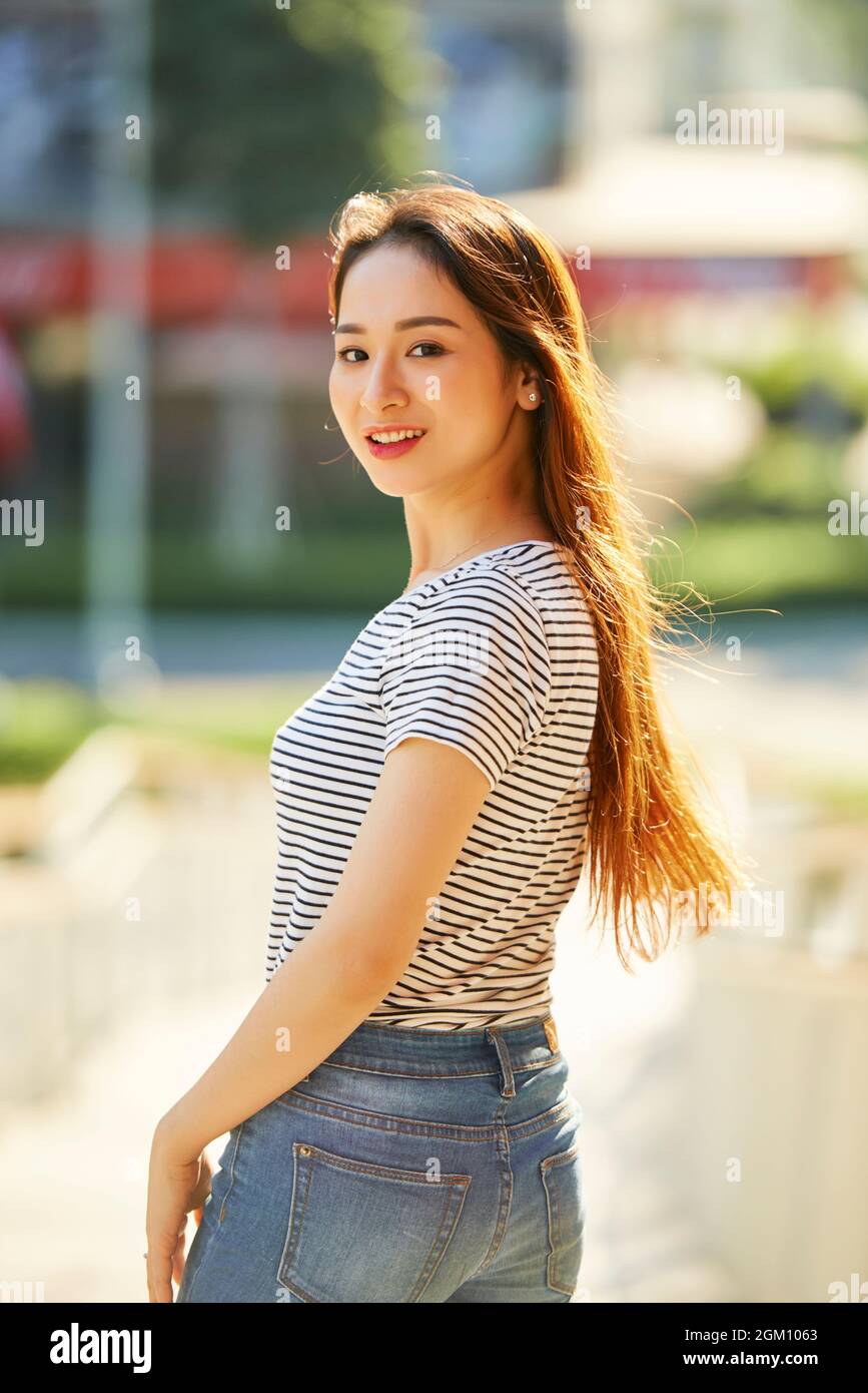 Portrait of smiling pretty young woman in striped t-shirt turning back ...