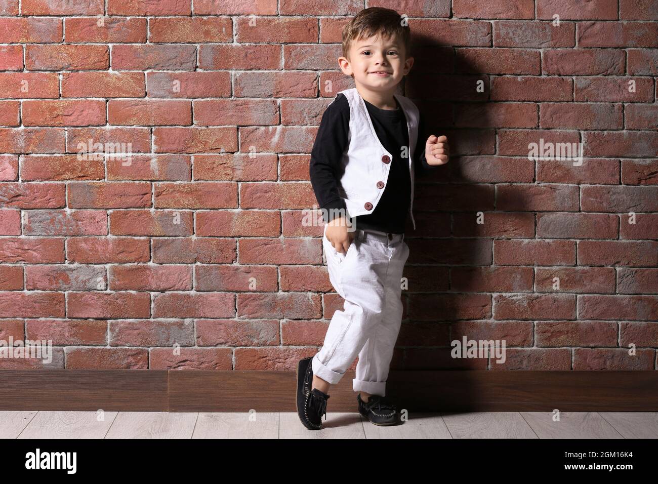 Adorable little boy standing near brick wall Stock Photo - Alamy