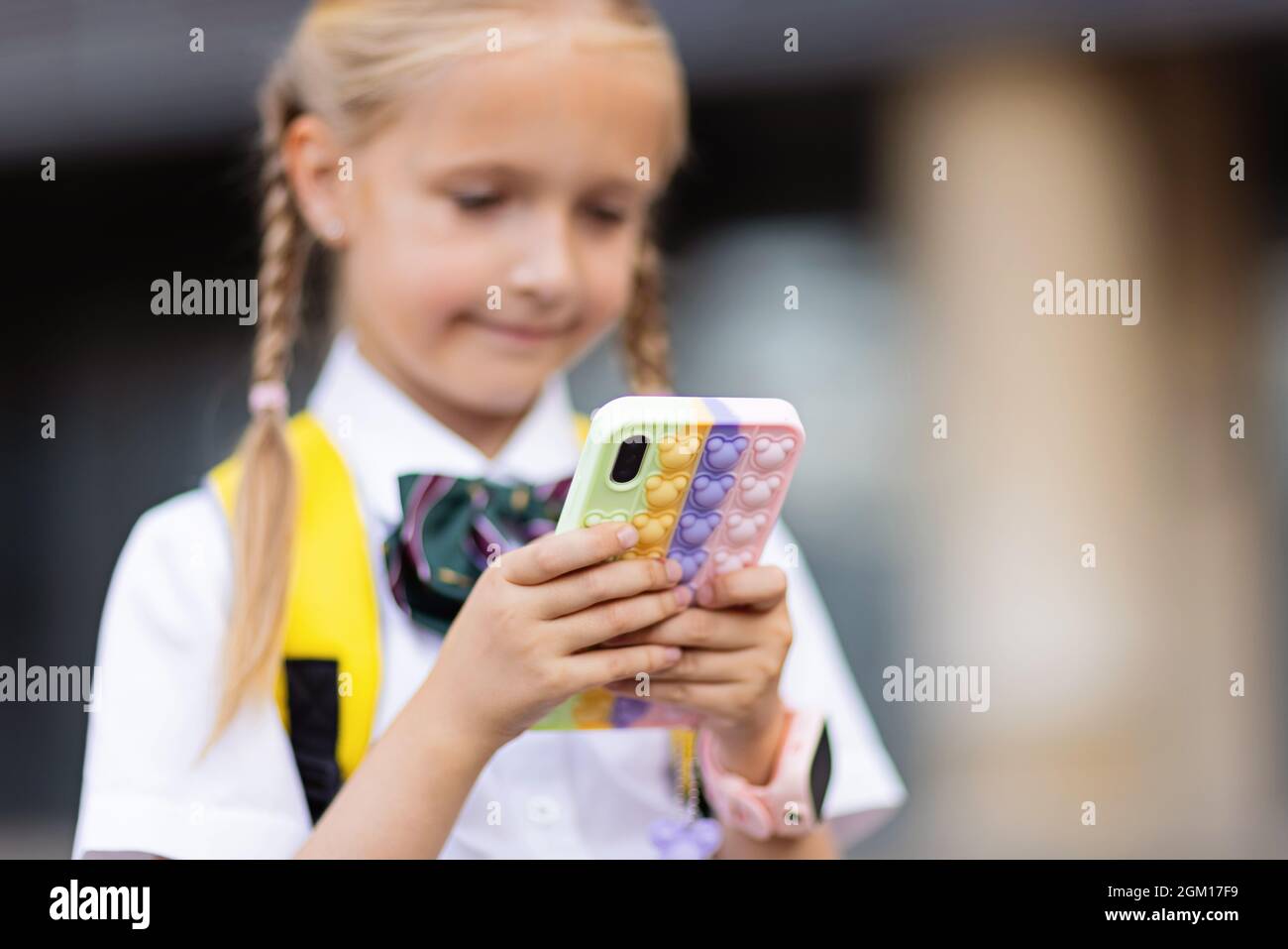 little caucasian girl is playing with mobile phone in new pop it toy ...
