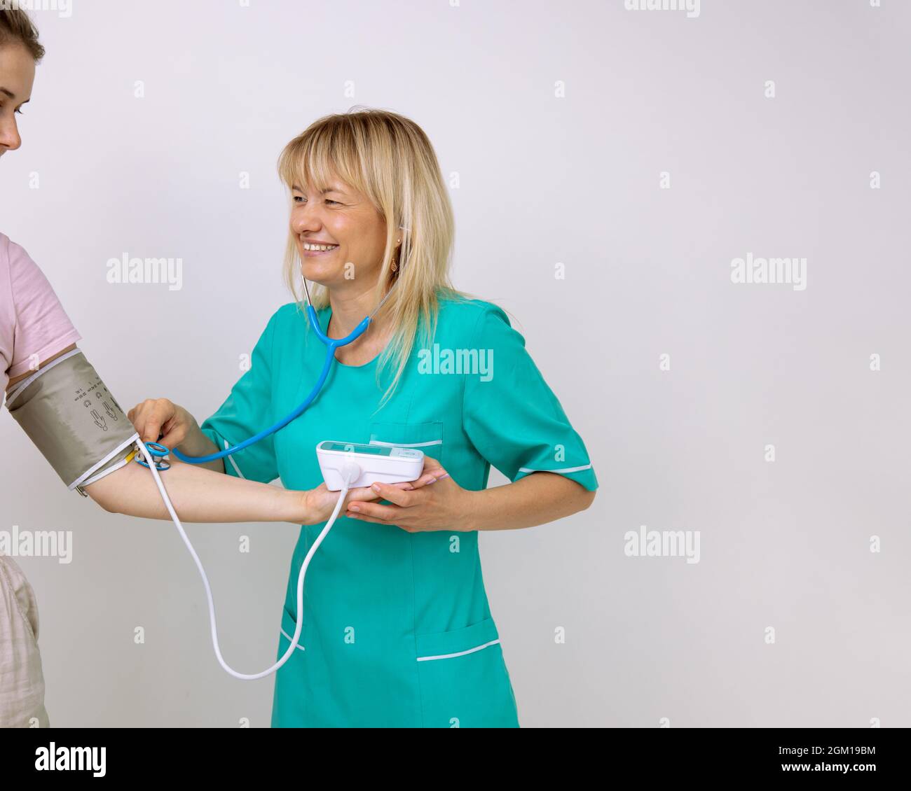 Positive female doctor in turquoise medical uniform measures patient's ...