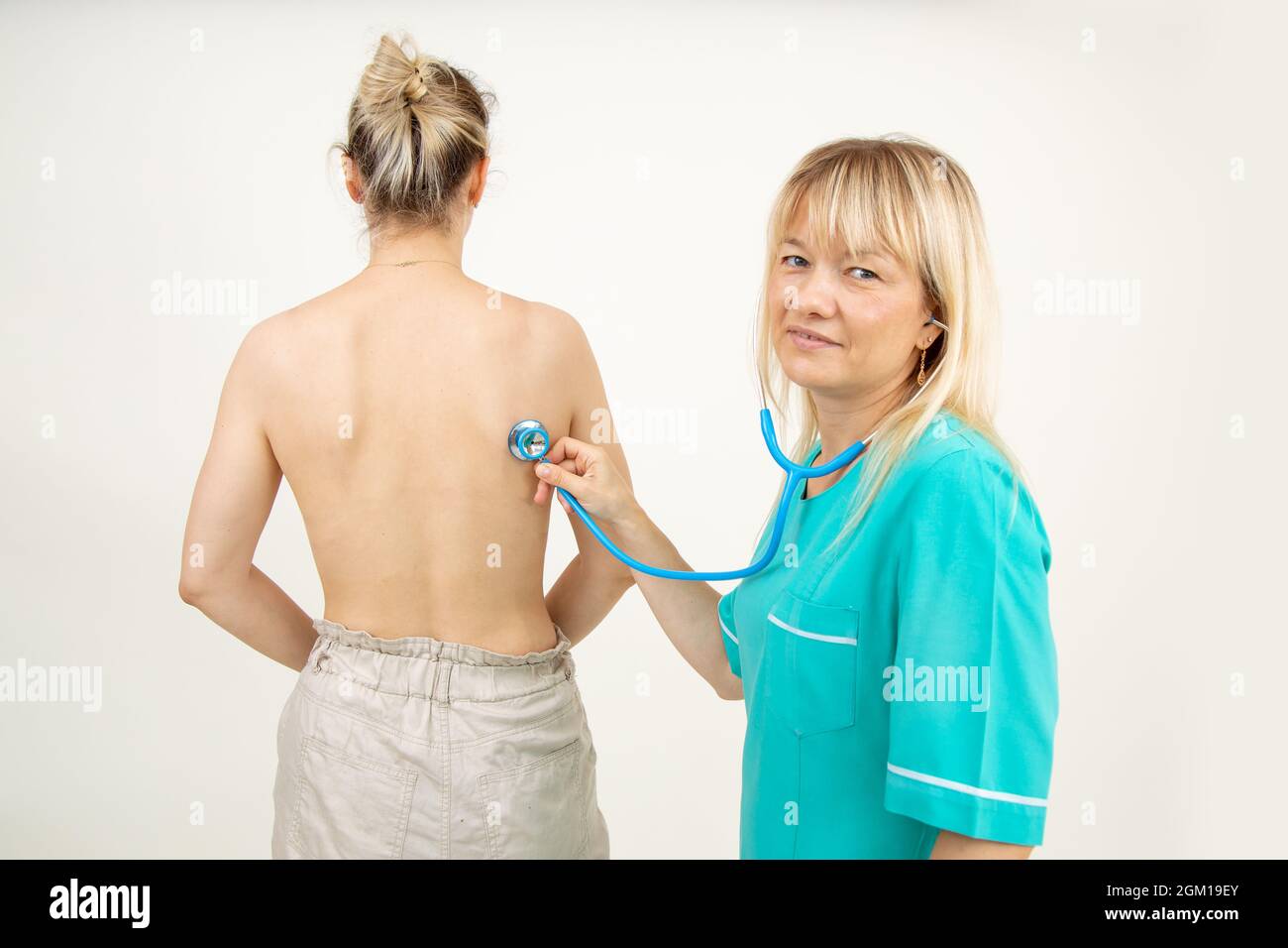Attractive blonde doctor in turquoise medical uniform conducts medical ...