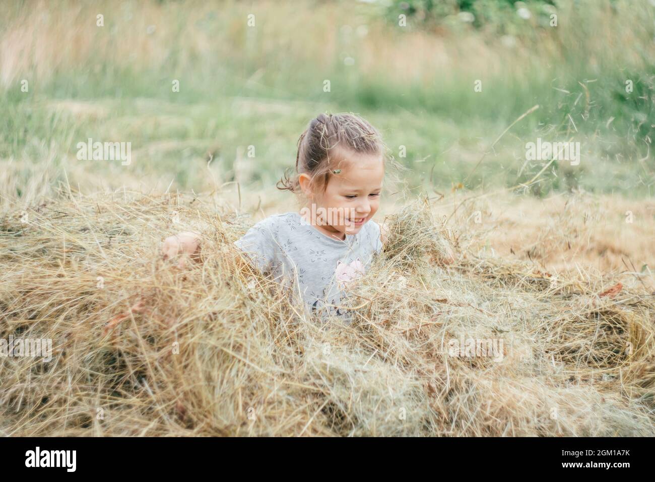 Little girl 3-4 years old jumps and plays in hay stack, throwing it up ...