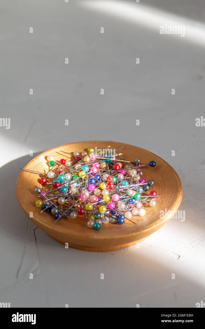 colored sewing pins in a golden plate against grey background with ...