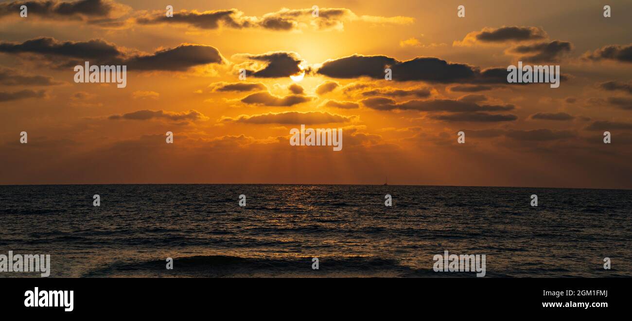 Sun rays emerge from the clouds, as the sun sets over the ocean ...