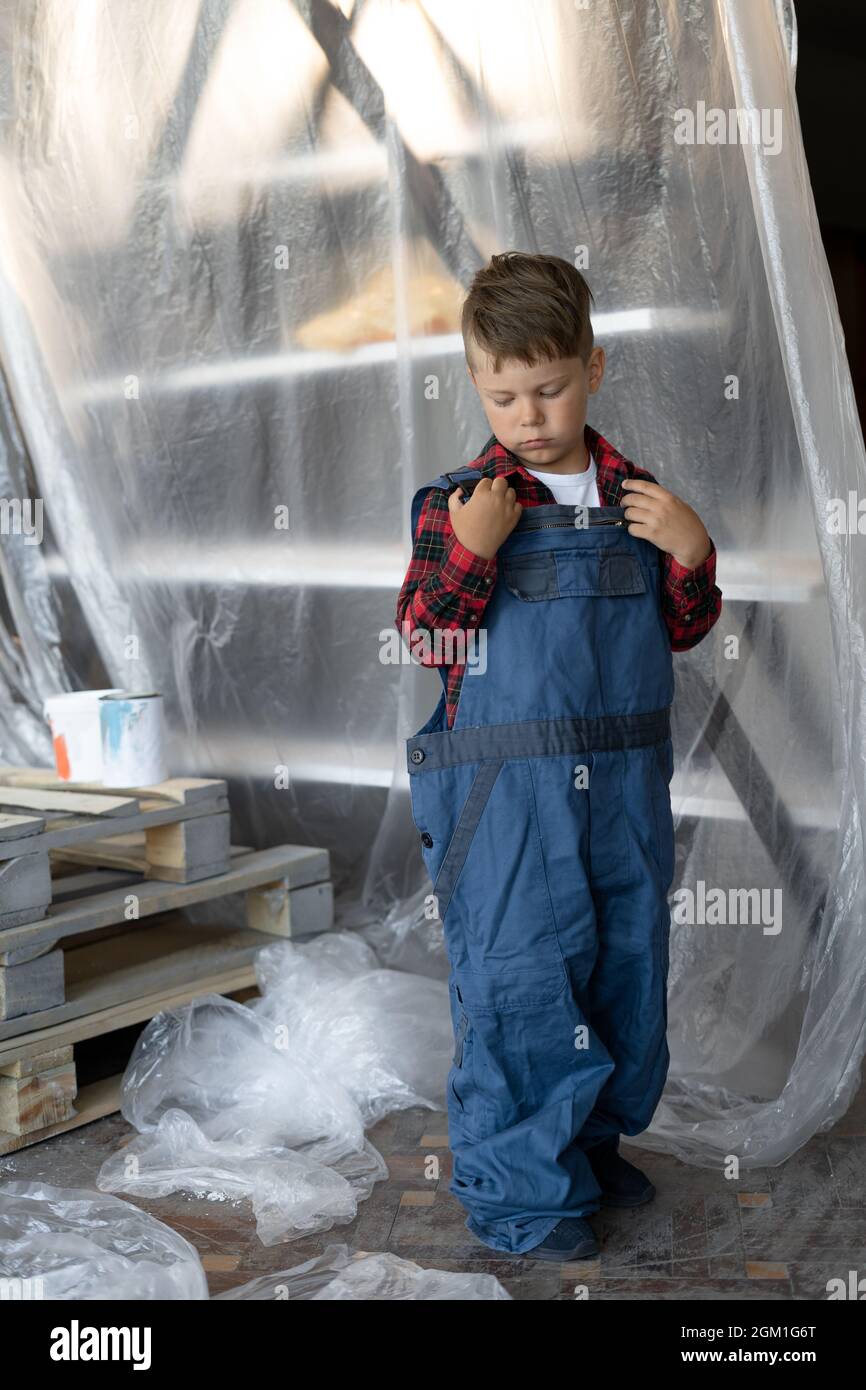 Boy builder. A child in a blue overalls at a construction site. Suit ...