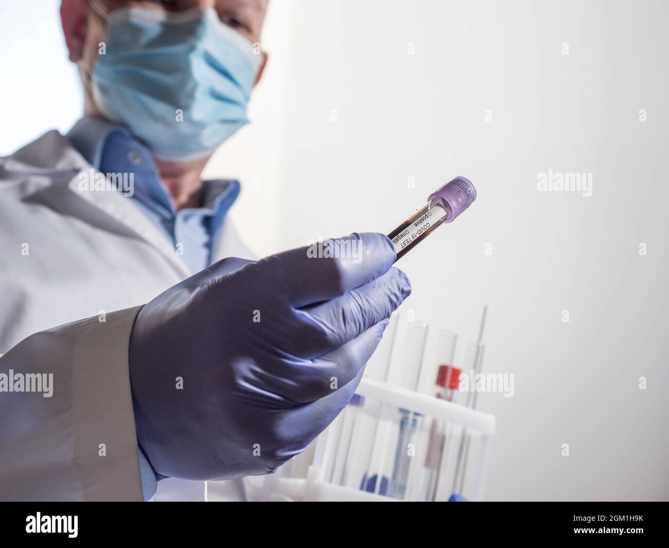 Doctor wearing mask and gloves checks a covid-19 analysis test tube ...