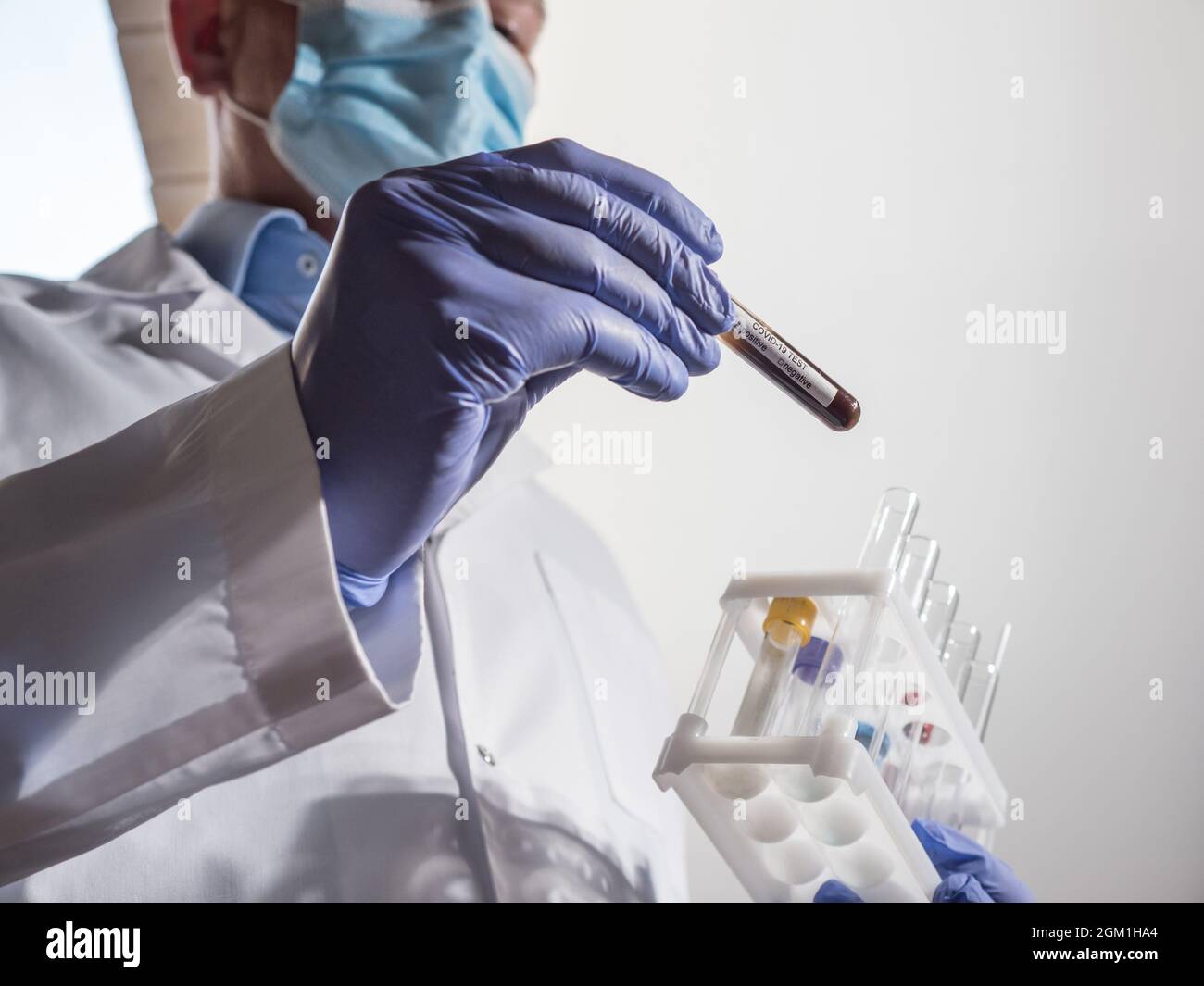 Doctor wearing mask and gloves checks a covid-19 analysis test tube ...