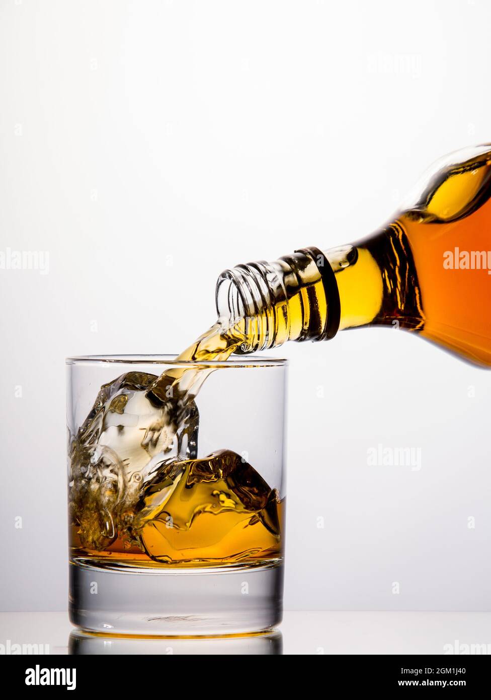 Pouring whisky from a bottle into a tumbler on white background Stock ...