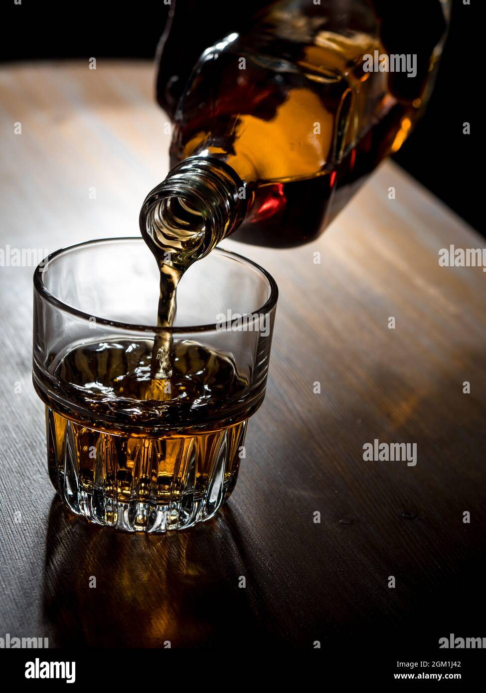 Man pouring whisky into a glass in a dark room Stock Photo - Alamy
