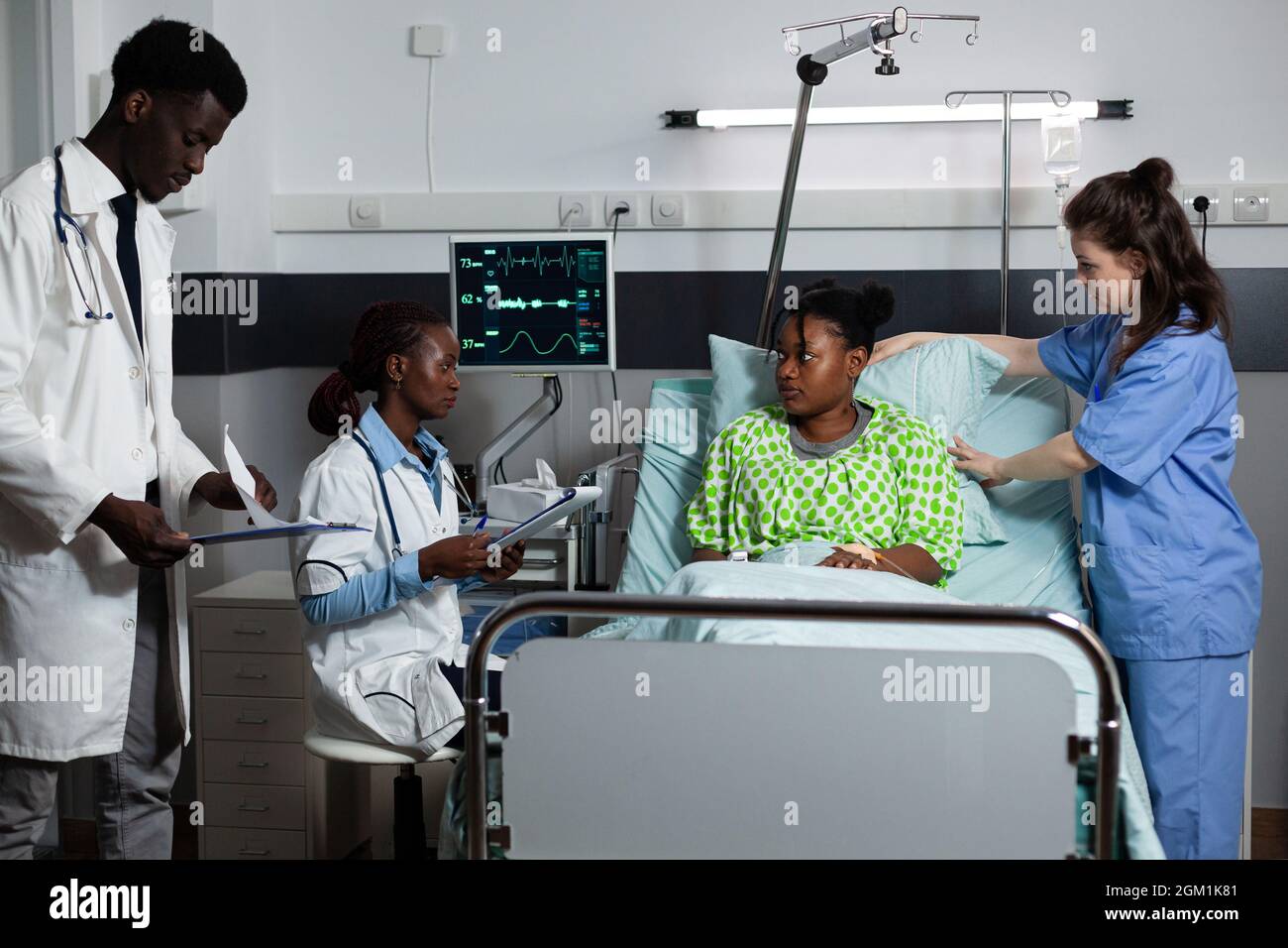 Multi ethnic medical team consulting young person in hospital ward bed ...