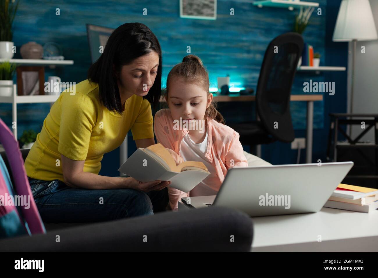 Mother assisting little child on reading school book while sitting at ...