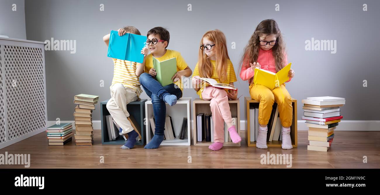 Group of children sitting on the book's stacks and on the bookshelves ...