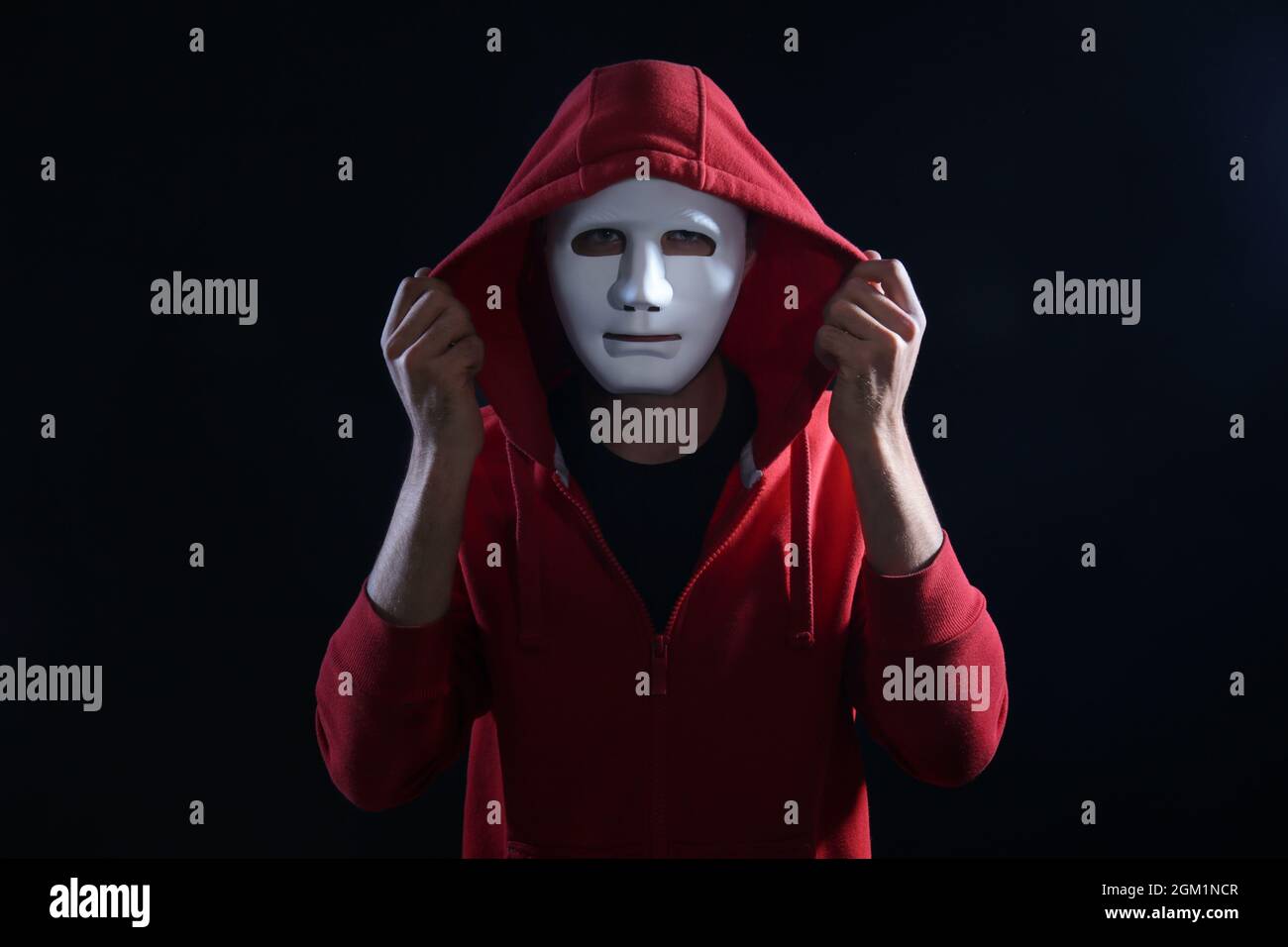 Masked hacker wearing hoodie in darkness Stock Photo - Alamy
