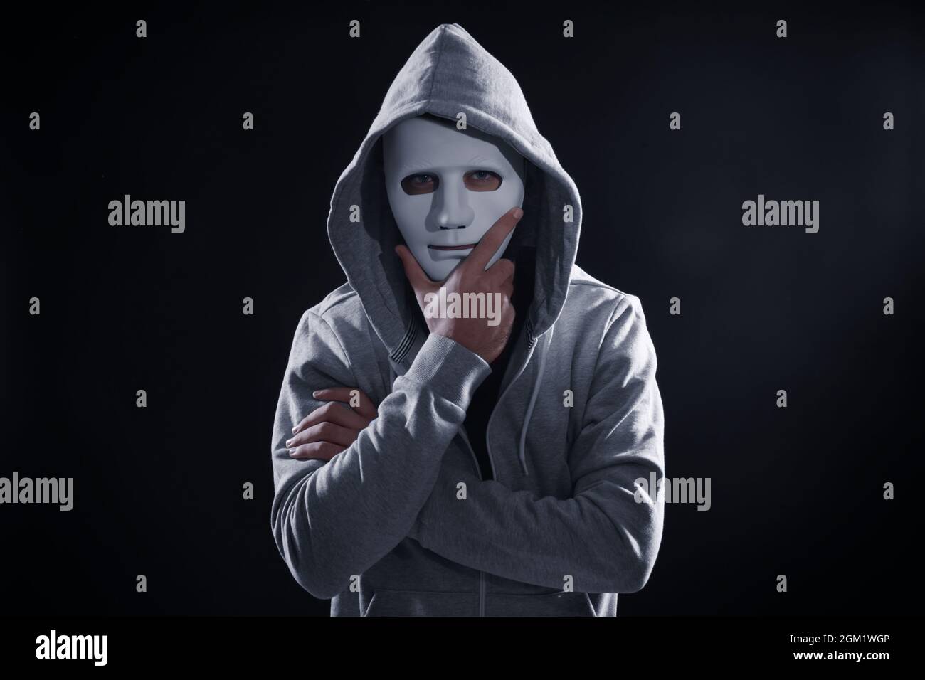 Masked hacker wearing hoodie in darkness Stock Photo - Alamy