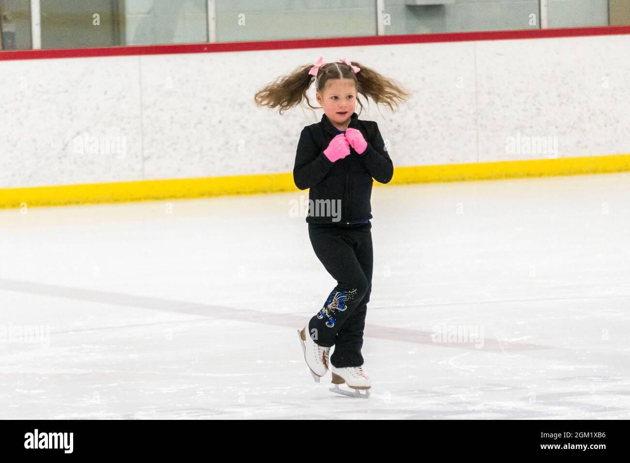 Little girl practicing figure skating moves on the indoor ice rink ...