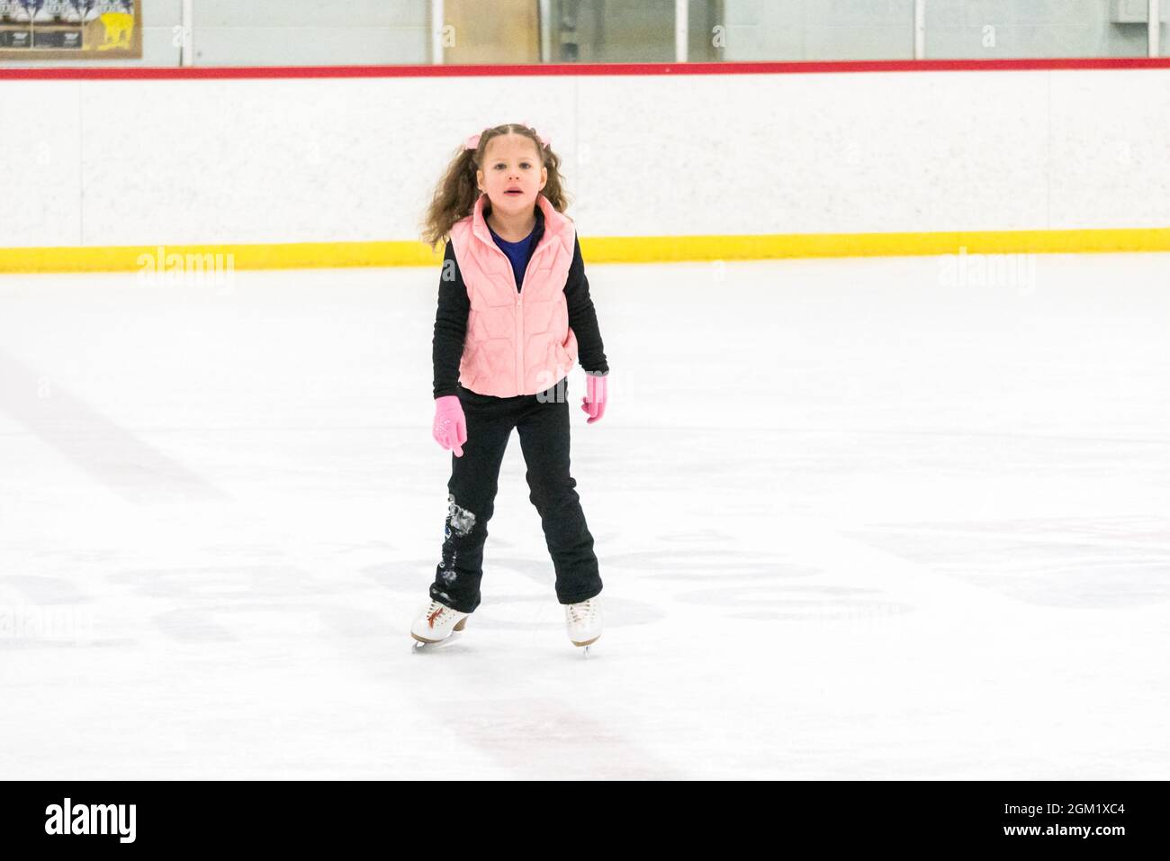 Little girl practicing figure skating moves on the indoor ice rink ...