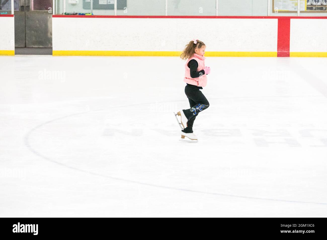 Little girl practicing figure skating moves on the indoor ice rink ...