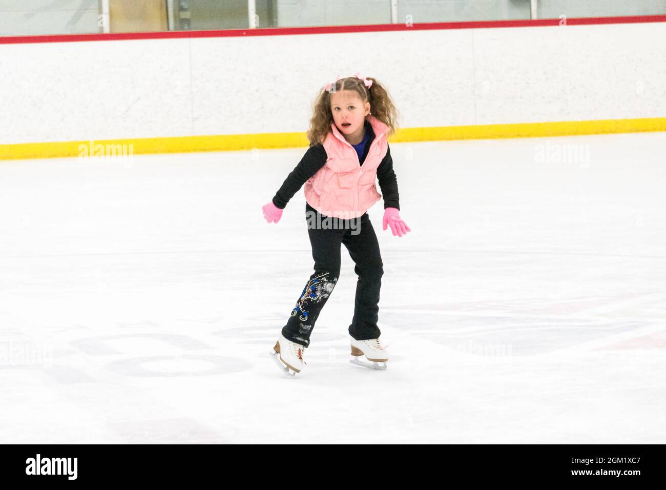 Little girl practicing figure skating moves on the indoor ice rink ...
