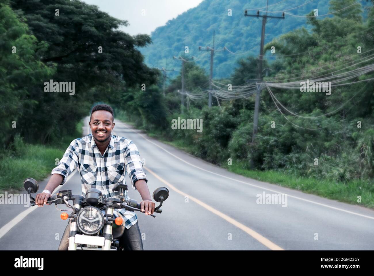 African biker man in the helmet riding a motorcycle rides on highway ...