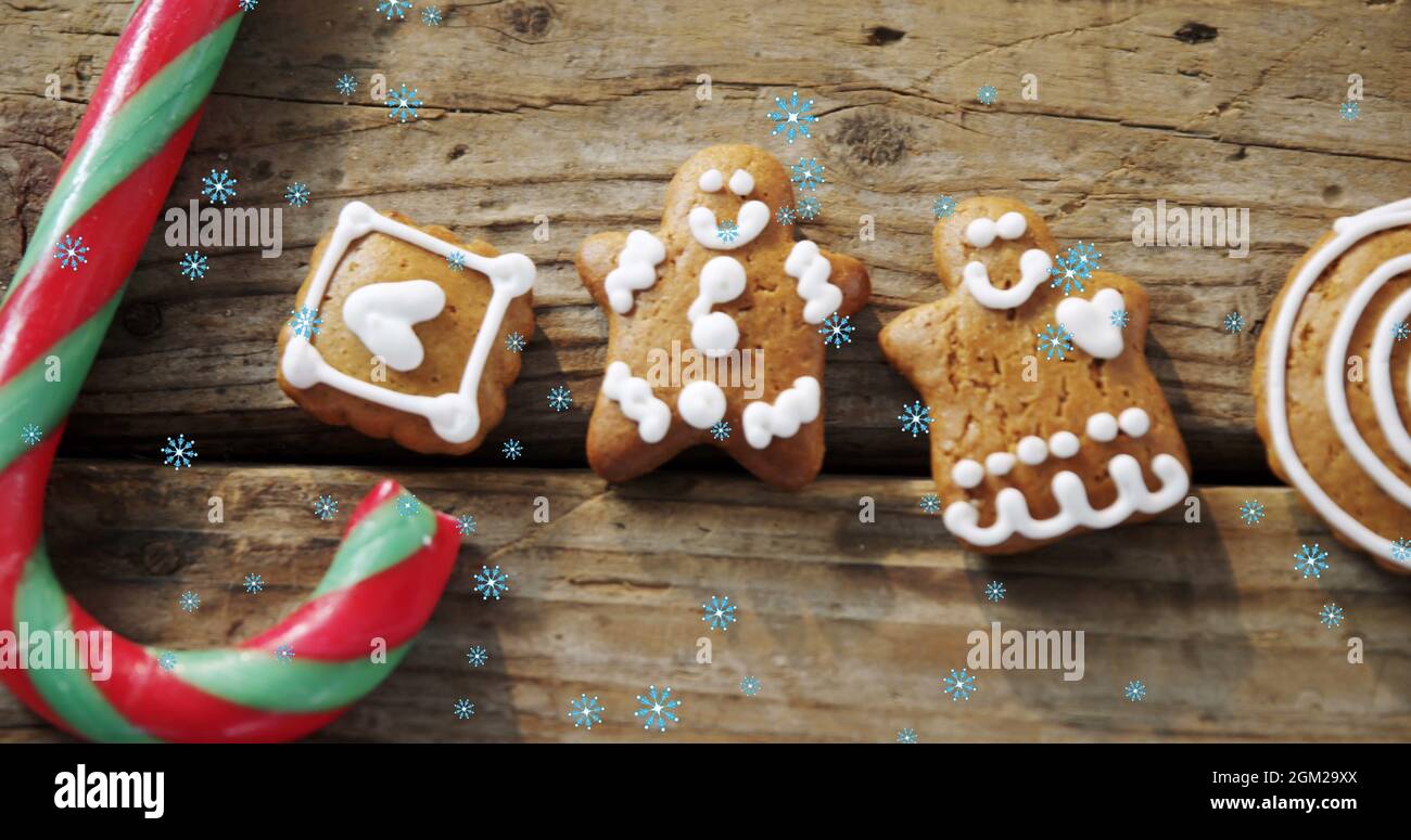 Snowflakes falling against gingerbread man cookies and candy cane on ...