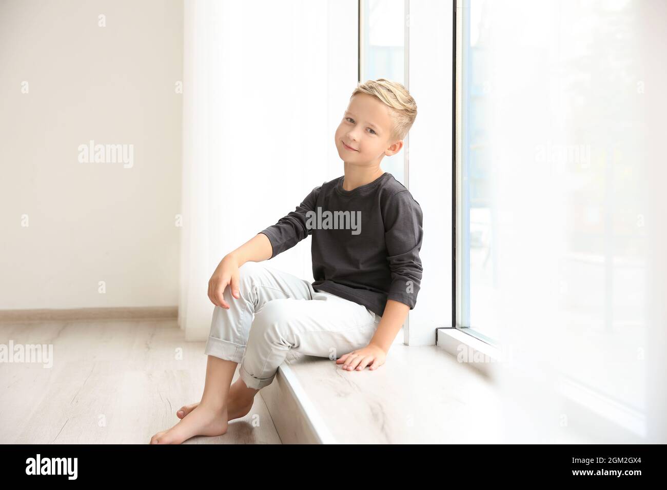 Cute little boy sitting near window at home Stock Photo - Alamy