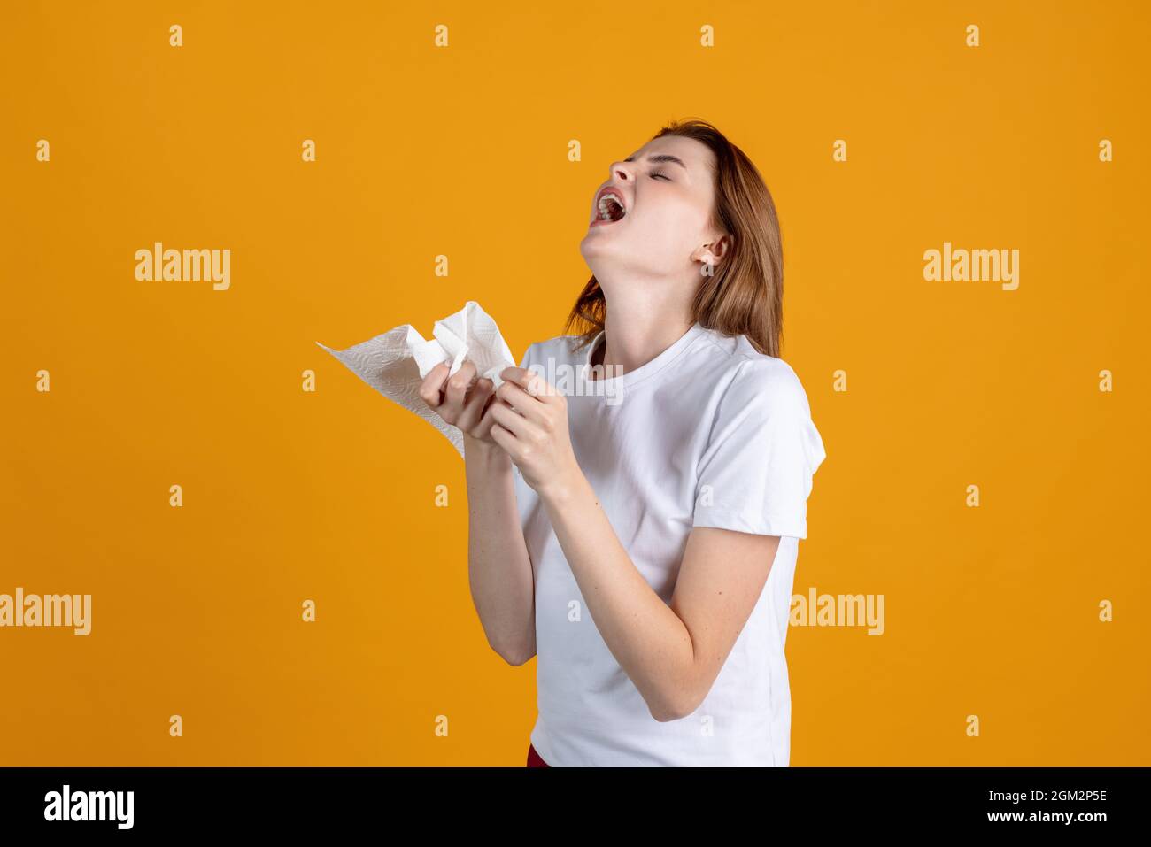 One young girl sneezing, having a runnynose isolated on yellow color ...