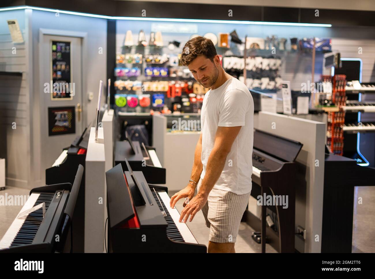 Side view of young male customer touching keys of electronic piano ...