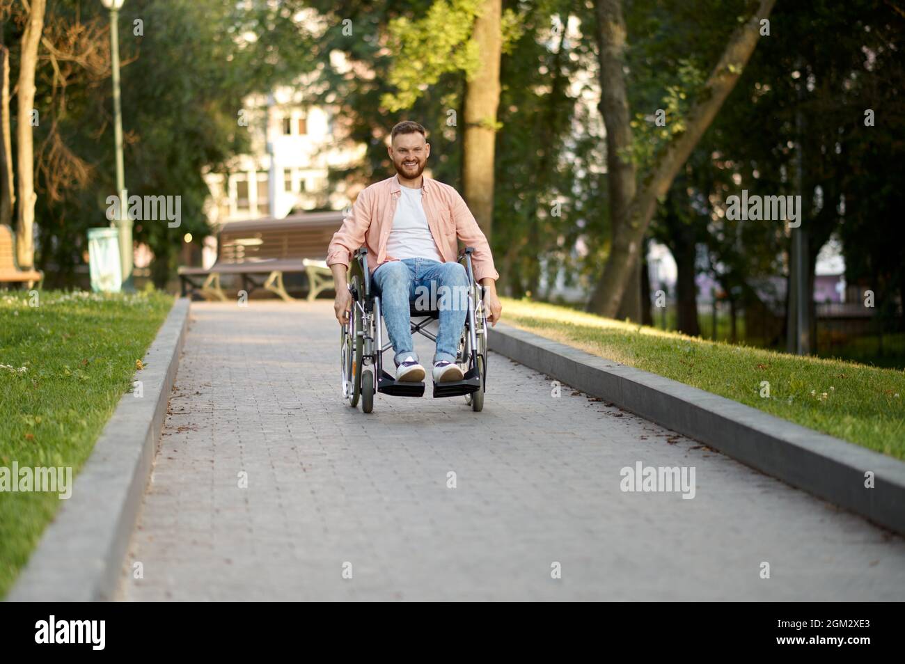 Disabled man in wheelchair rides on a path in park Stock Photo - Alamy