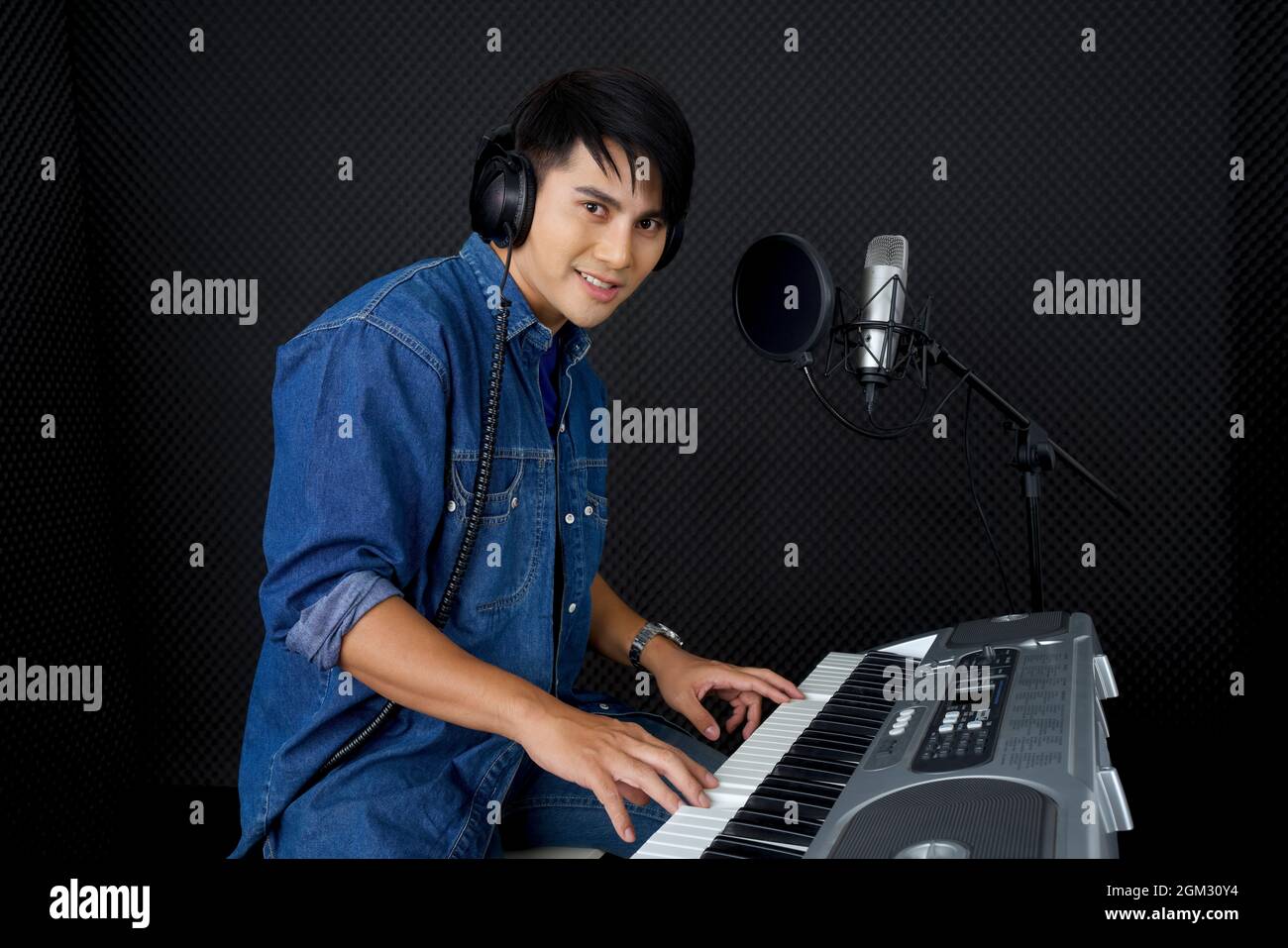 Young asian man with headphones playing an electric keyboard in front ...
