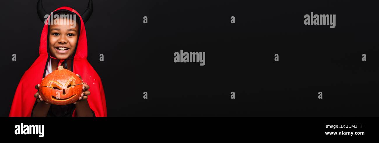 happy african american boy in devil halloween costume holding carved ...
