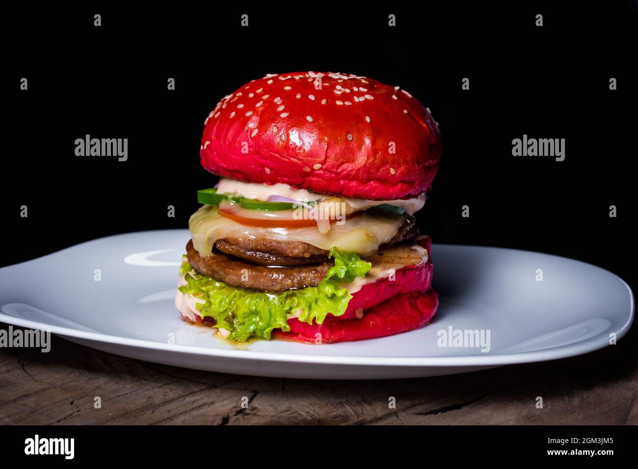 Delicious red cheeseburger on a white plate on a tree trunk on a black ...