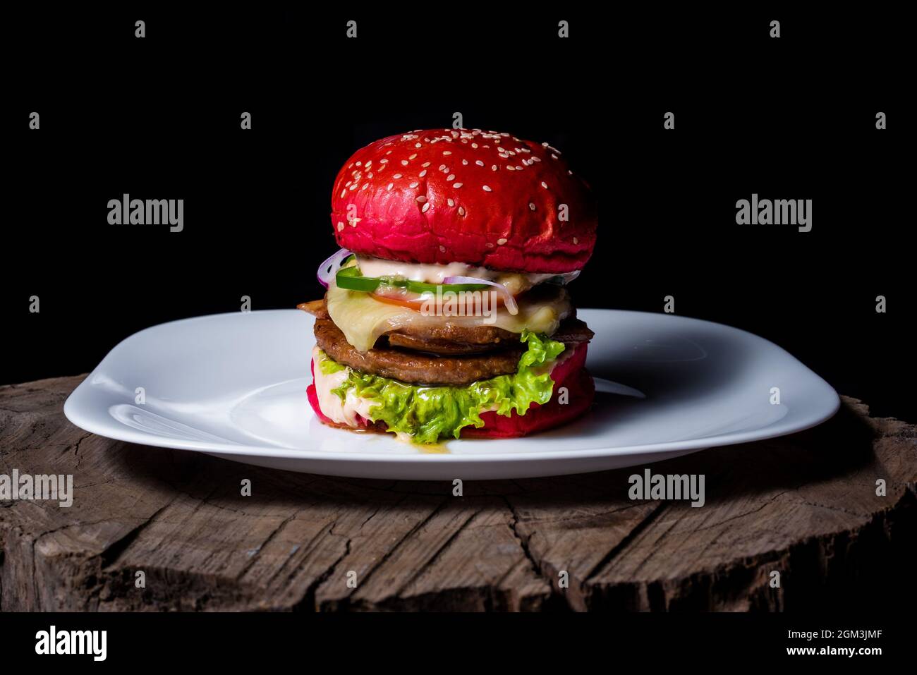 Delicious red cheeseburger on a white plate on a tree trunk on a black ...