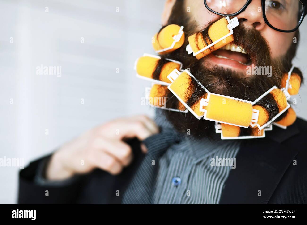 Cheerful hipster man with curlers in beard. Surprised man with glasses ...