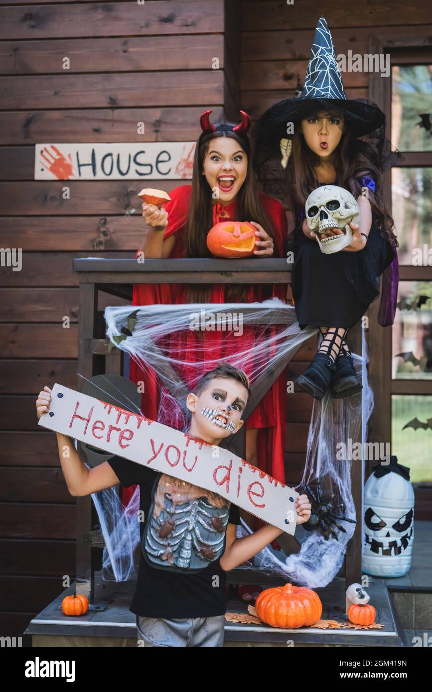 boy with scary grimace holding card with here you die lettering near ...
