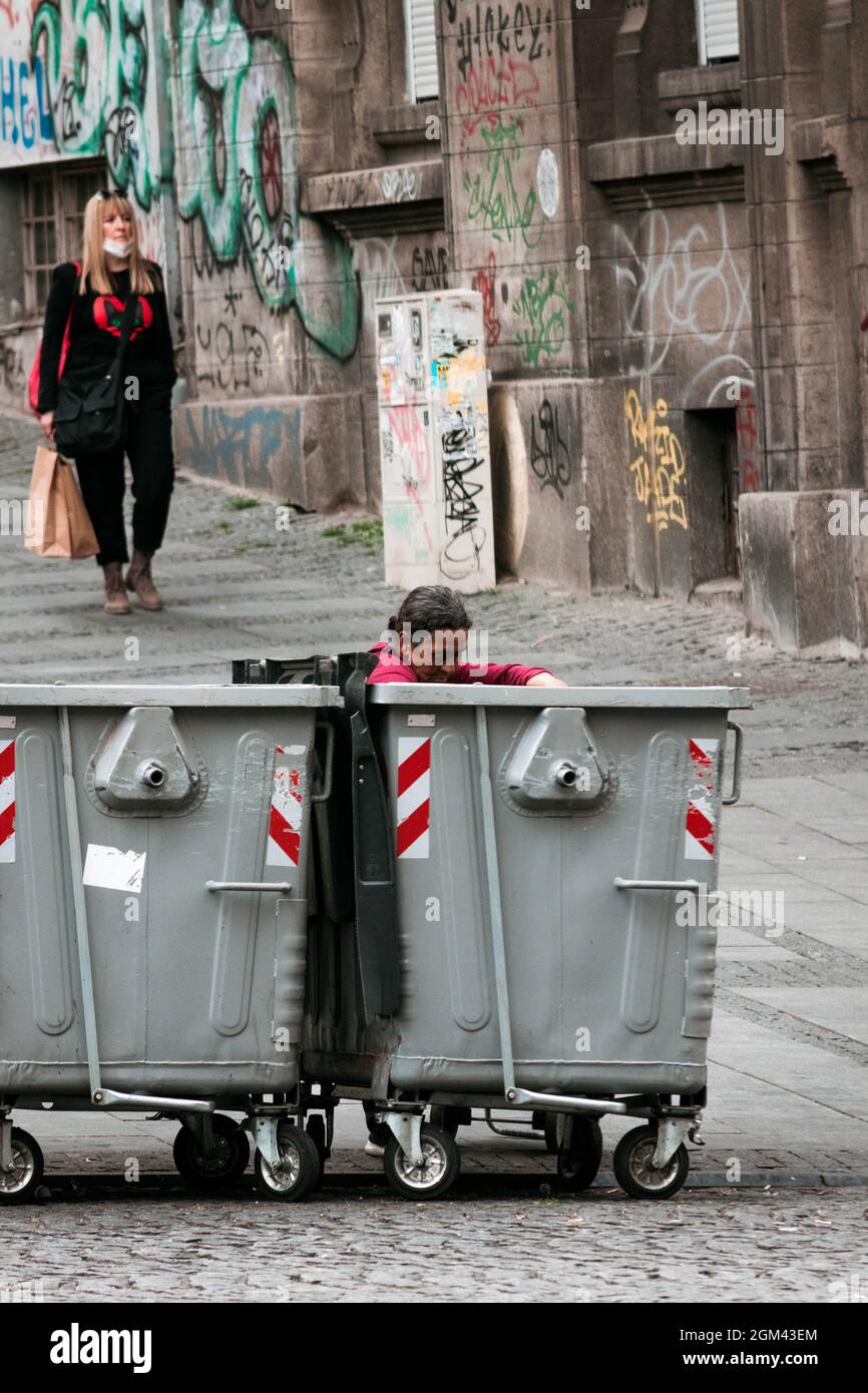 A poor gypsy woman digging through a thrash container on the street ...