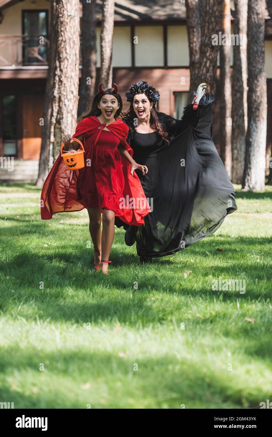 excited woman and girl in halloween costumes screaming while running in ...