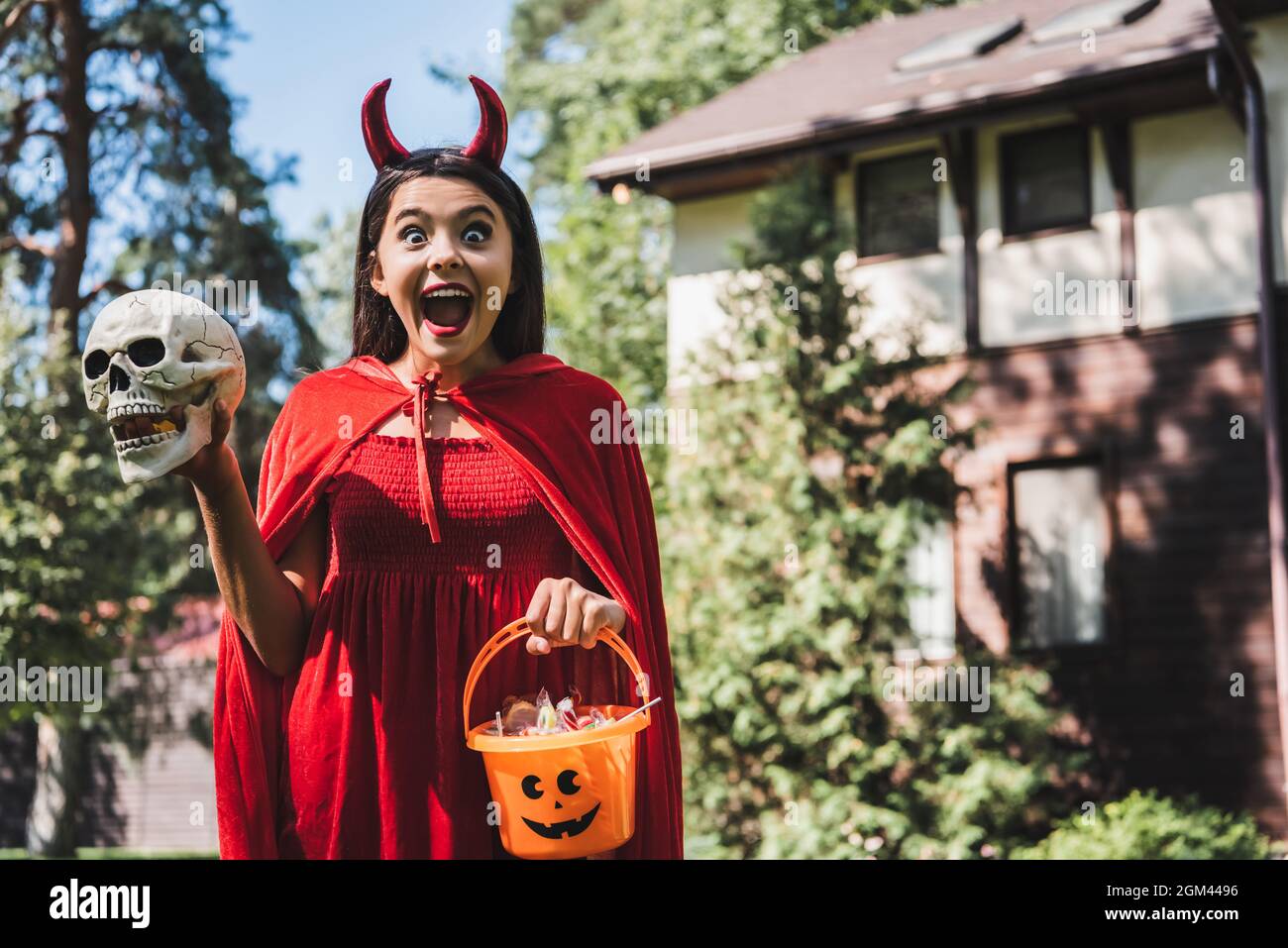 astonished child in demon costume screaming while holding skull and ...