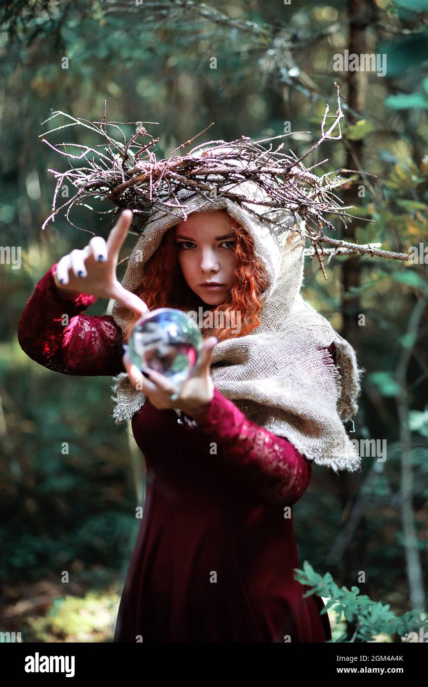 The red-haired witch holds a ritual with a crystal ball in the forest ...