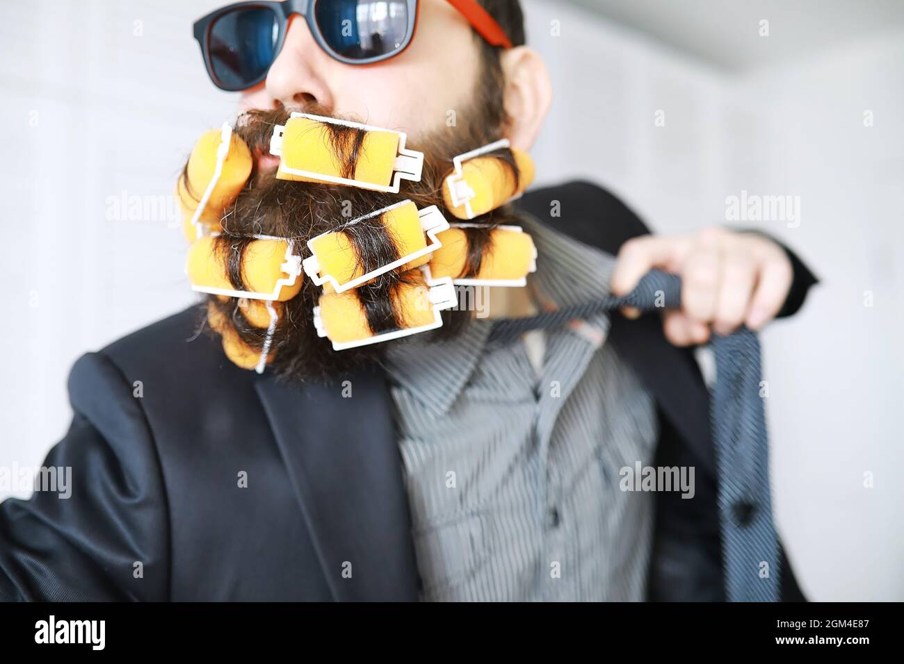 Cheerful hipster man with curlers in beard. Surprised man with glasses ...