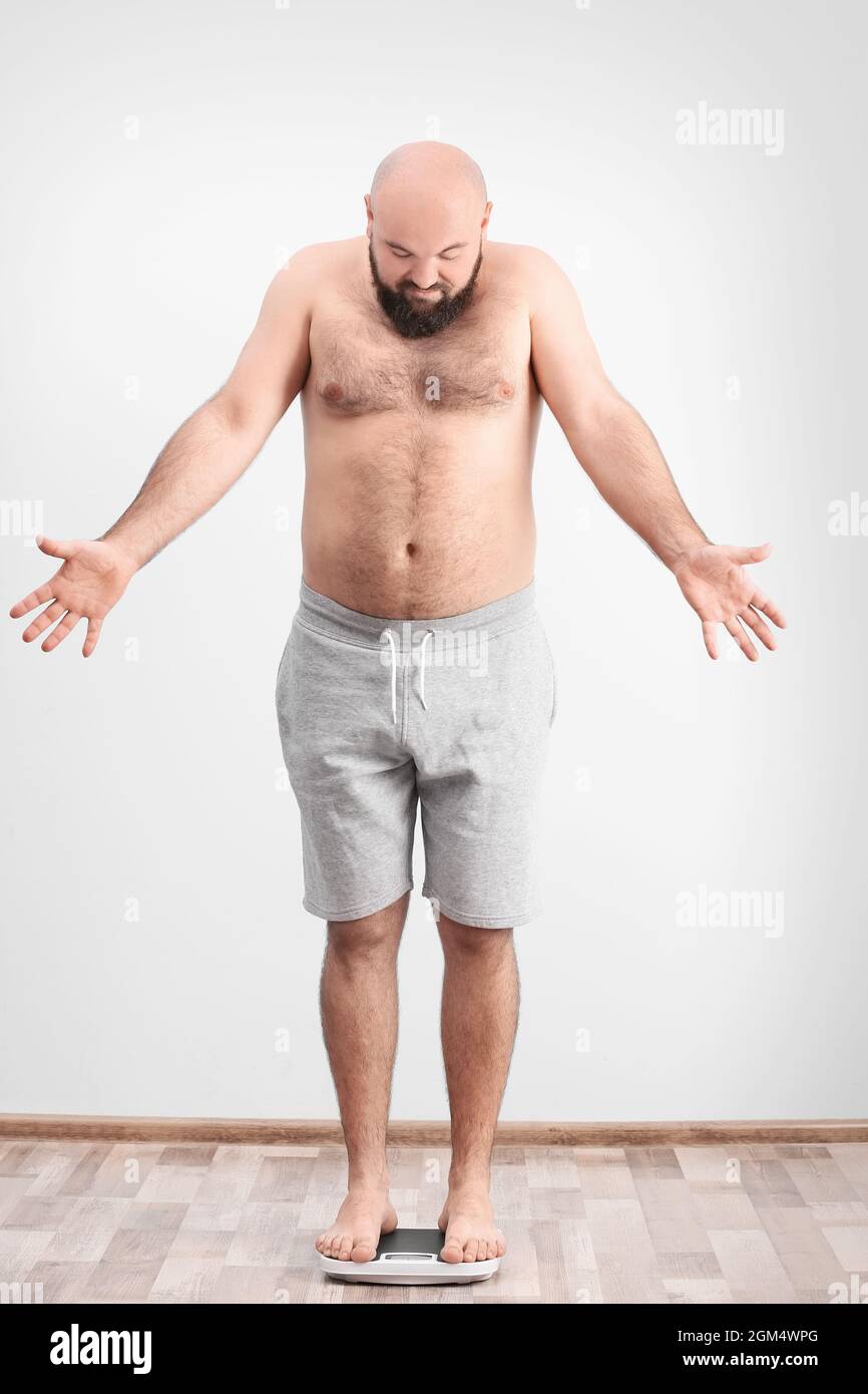 Overweight man measuring his weight using scales on floor Stock Photo ...