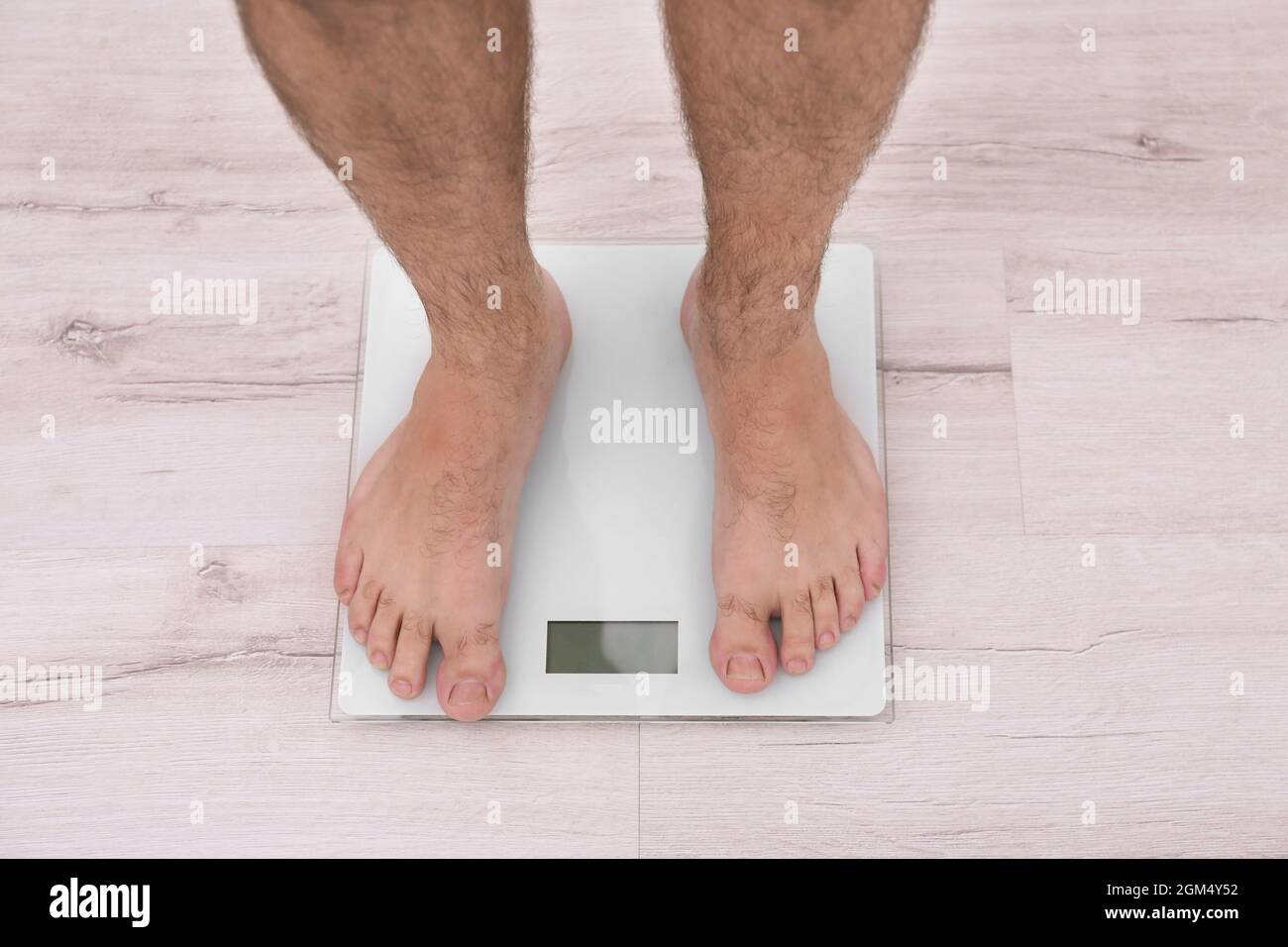 Overweight man measuring his weight using scales on floor Stock Photo ...