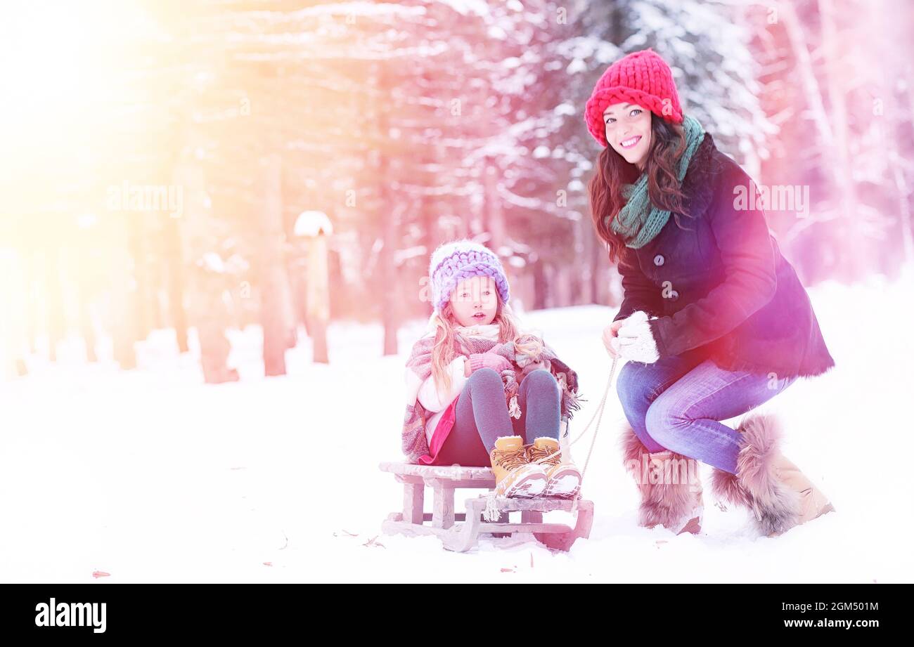 Winter fairy tale, a young mother and her daughter ride a sled in the ...