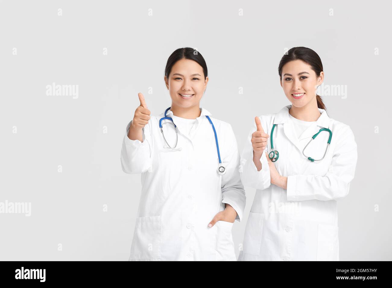 Portrait of female Asian doctors showing thumb-up on light background ...