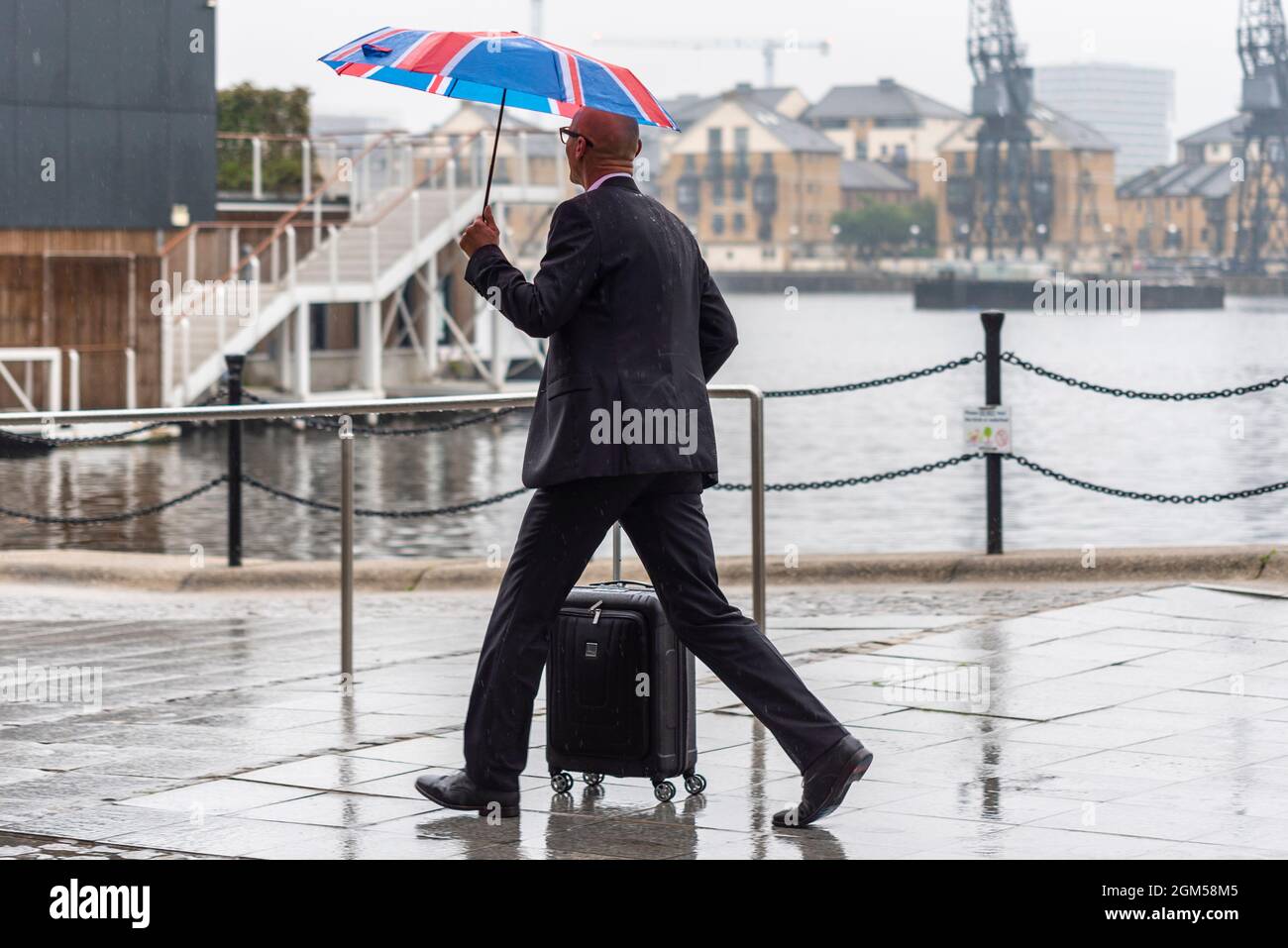 A businessman in a suit carrying a Union Jack flag umbrella and ...