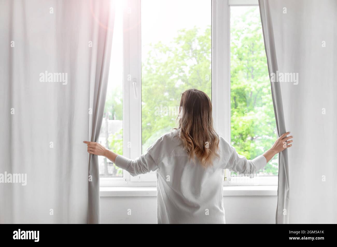Woman opening light curtains in modern room Stock Photo - Alamy