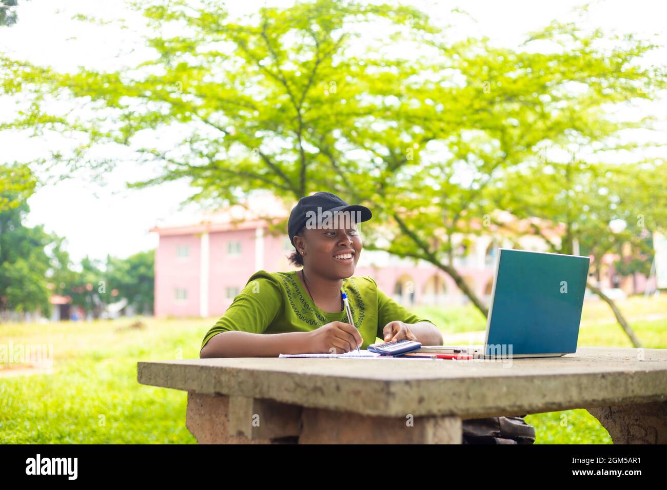 Pretty female student happily doing her assignment in the campus park ...