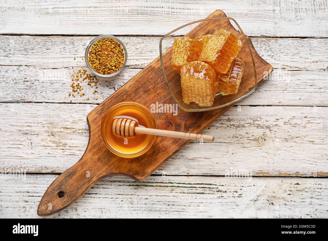 Bowls of honey, combs and bee pollen on white wooden background Stock ...