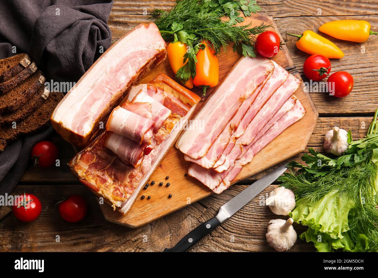 Board with tasty smoked bacon and fresh vegetables on wooden background ...