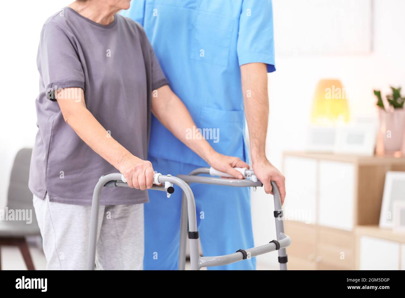 Senior woman walking with assistance of young caregiver indoors Stock ...