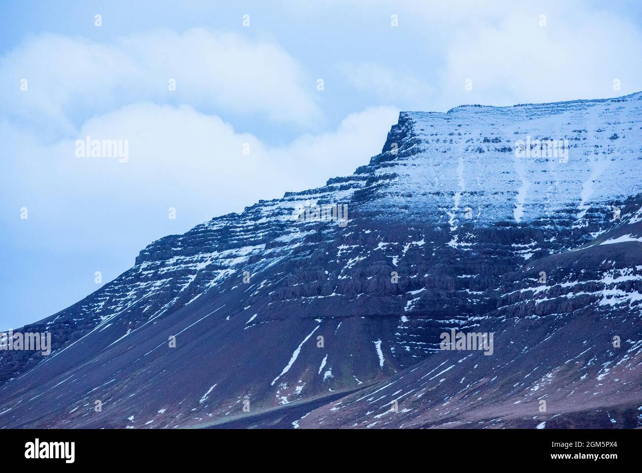 Snow capped black mountain ridges in Iceland with clouds to add depth ...